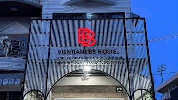 Um hostel com um logo 'BB' em destaque, uma varanda com grades ornamentadas e uma entrada bem iluminada.