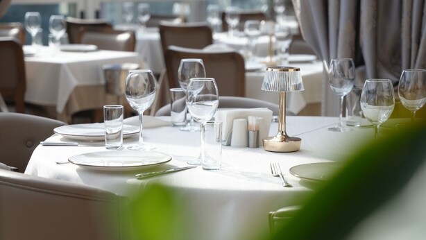 Restaurante com mesas preparadas para refeições, oferecendo vista da cidade através de grandes janelas.