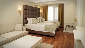 Quarto de hotel com cama grande, sofá, poltrona e mesa de cabeceira.