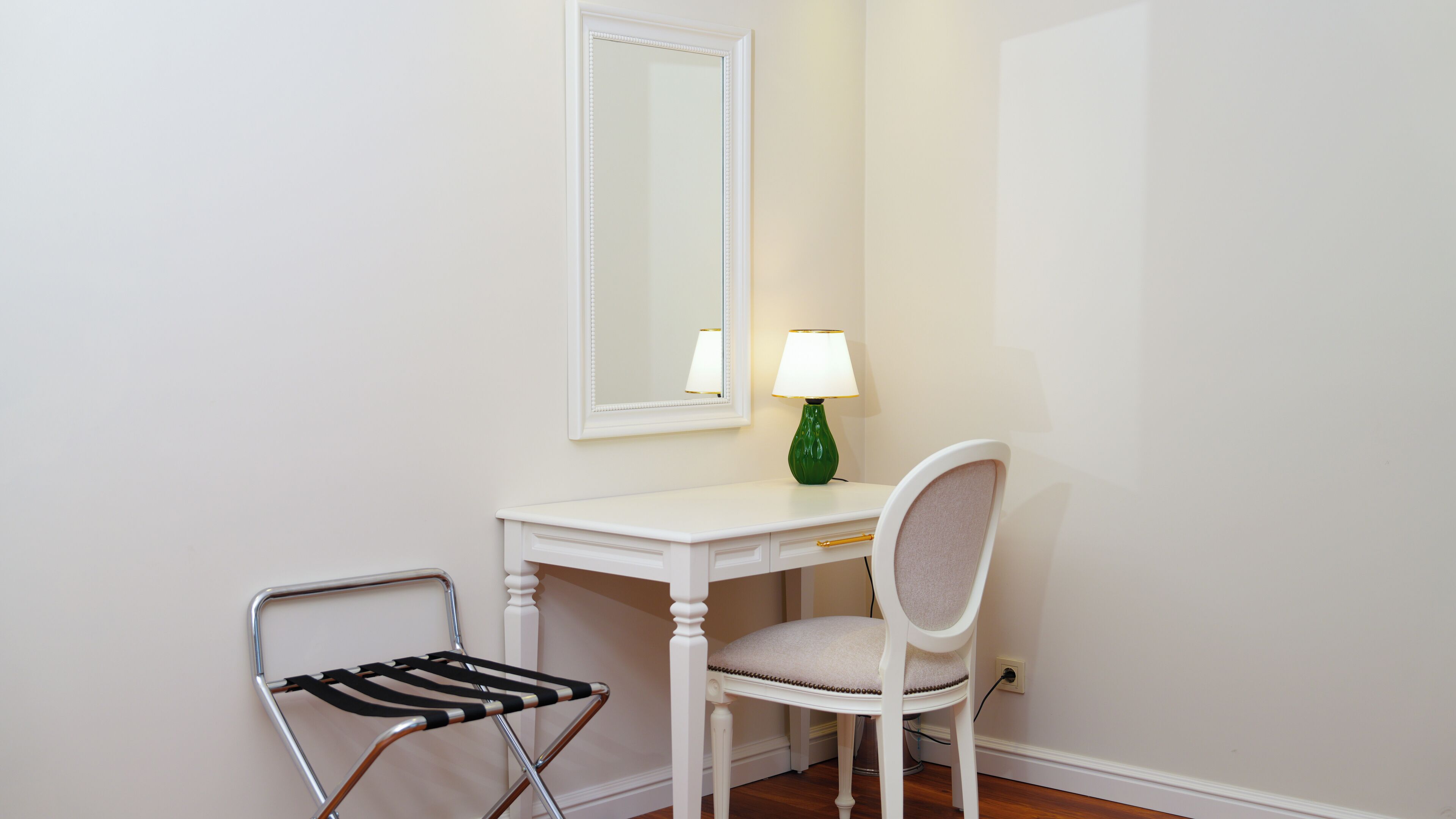 Um quarto pequeno e branco, com uma escrivaninha, cadeira e espelho.