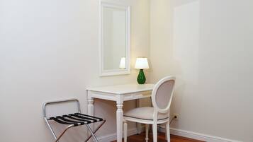 Um quarto pequeno e branco, com uma escrivaninha, cadeira e espelho.