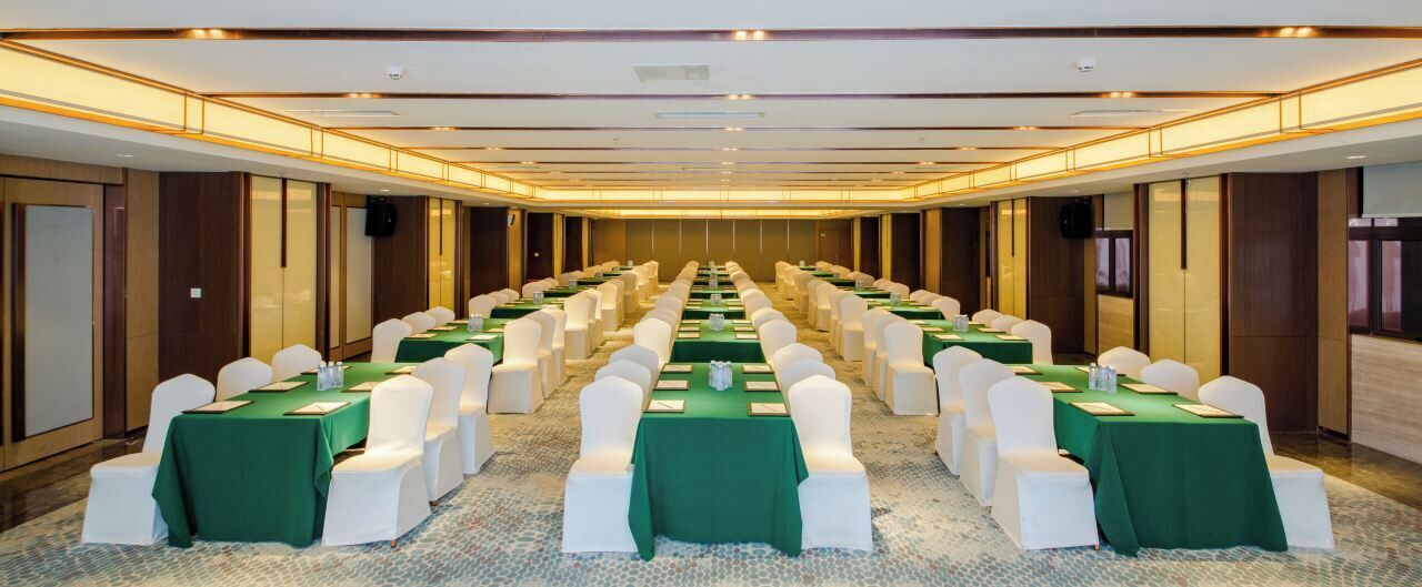 Uma sala de conferências com fileiras de mesas e cadeiras, equipada com placas de identificação e garrafas de água.