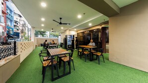 Um restaurante com mesas, cadeiras, um ventilador de teto e uma máquina de vendas.
