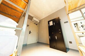 Quarto de hotel com teto de madeira, porta branca, cofre preto e pia branca.