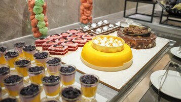 Buffet variado com diversas sobremesas, incluindo bolos, brownies e copas de frutas.