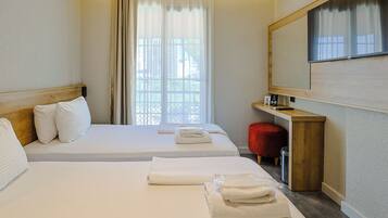 Quarto de hotel com duas camas, cabeceira de madeira, um banquinho vermelho, uma mesinha e uma televisão fixada na parede.