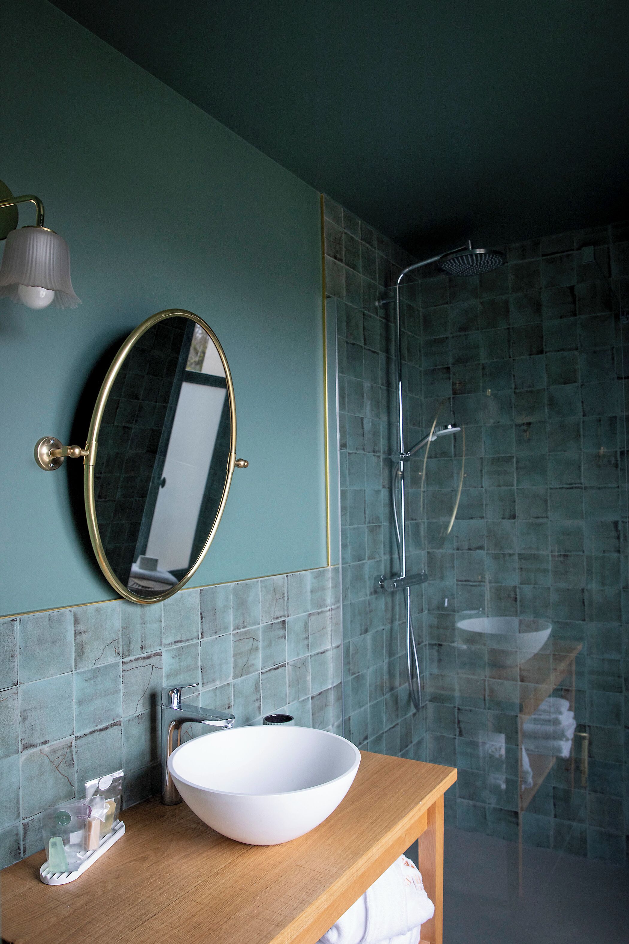 Casa de banho com um espelho oval grande, uma sanita branca e uma cabine de duche com porta de vidro.