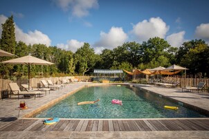 Piscina retangular com água cristalina, rodeada por cadeiras de descanso e guarda-sóis, com um deck de madeira em primeiro plano.
