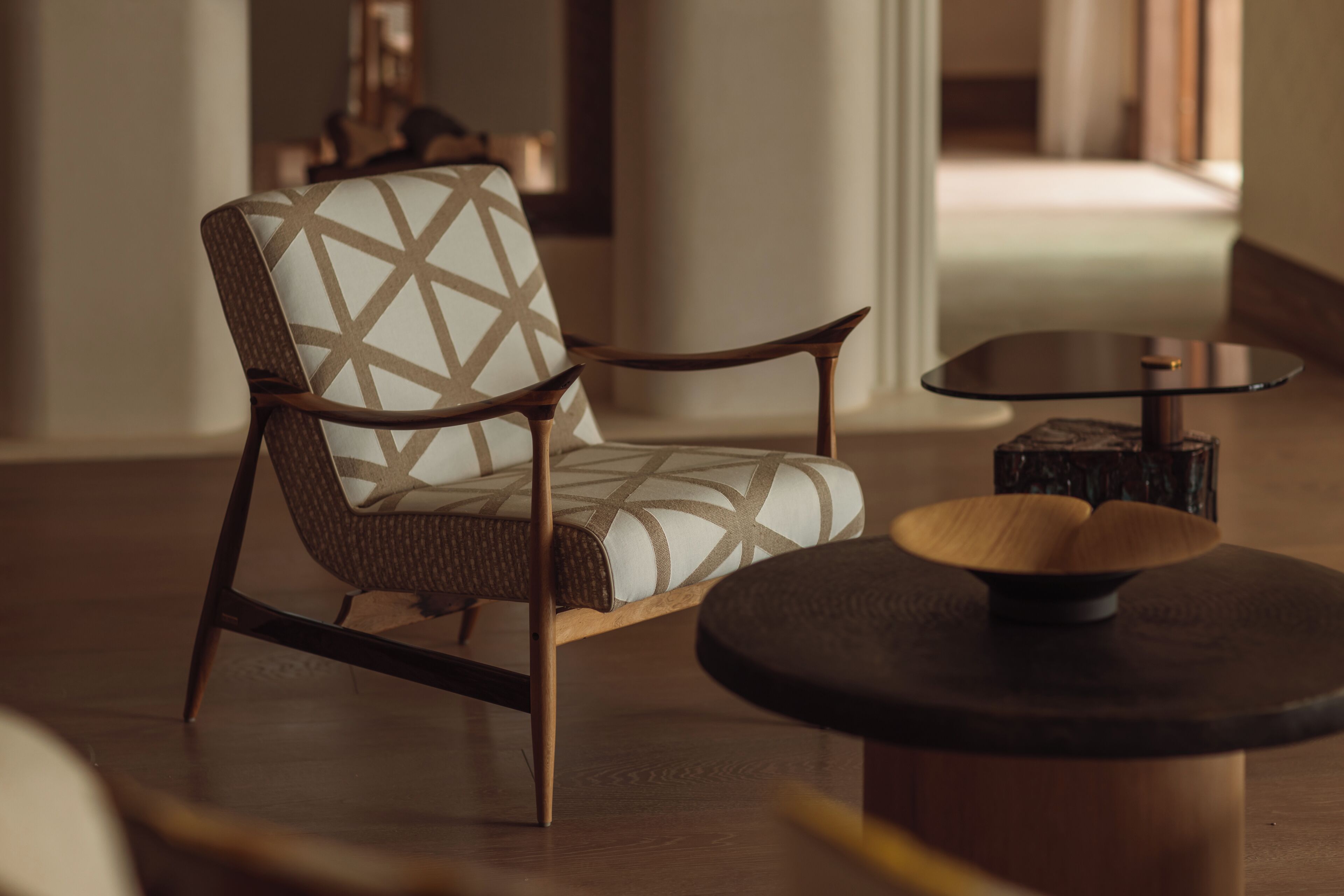 Uma área de estar moderna com uma poltrona estampada, uma mesa redonda de madeira e um bloco decorativo de madeira.