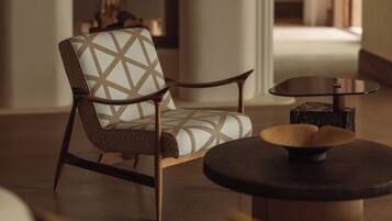 Uma área de estar moderna com uma poltrona estampada, uma mesa redonda de madeira e um bloco decorativo de madeira.