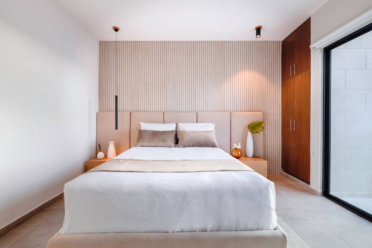 Quarto moderno com uma cama grande, um guarda-roupa de madeira e uma porta de vidro deslizante à direita.