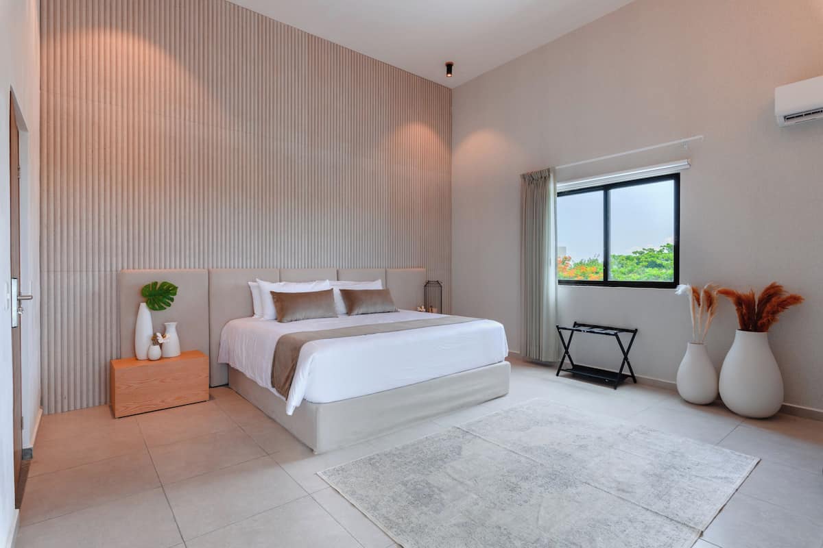 Quarto moderno com uma cama grande, uma mesa de cabeceira, cortinas e vista para o verde lá fora.