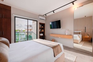 Quarto moderno com uma cama grande, TV fixada na parede, varanda com vista e prateleira de madeira com objetos decorativos.