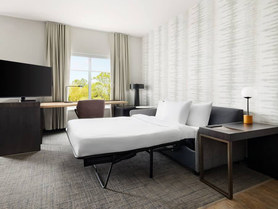 Quarto de hotel com cama, escrivaninha, televisão e abajur.