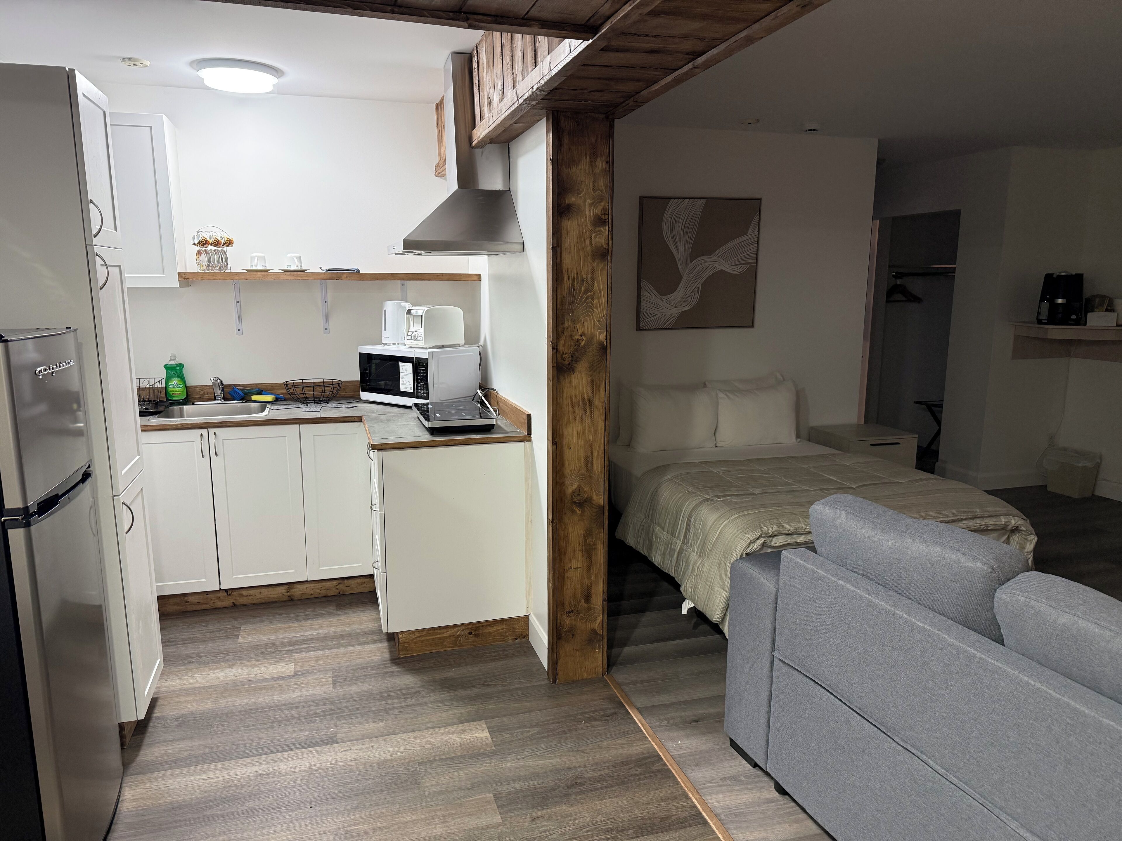 Um apartamento estúdio compacto com cozinha compacta, uma cama e um sofá cinzento.