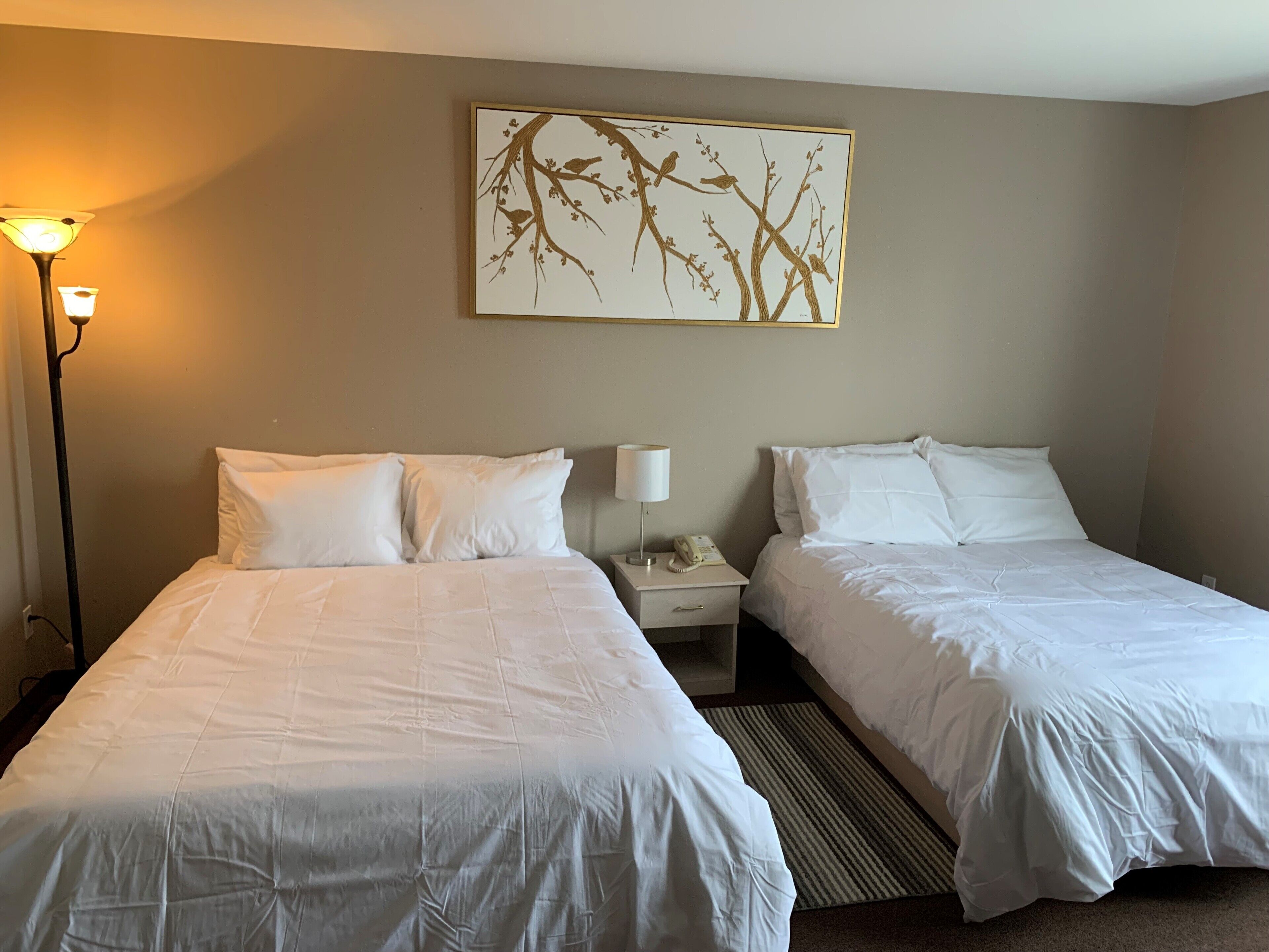 Quarto de hotel com duas camas, mesa de cabeceira com abajur e um quadro na parede.