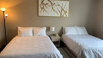 Quarto de hotel com duas camas, mesa de cabeceira com abajur e um quadro na parede.