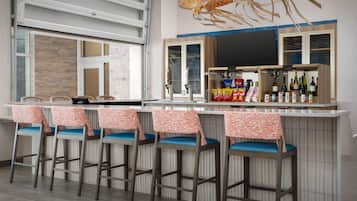 Uma área de bar com banquetas altas, uma grande decoração de caranguejo e diversas opções de petiscos e bebidas.