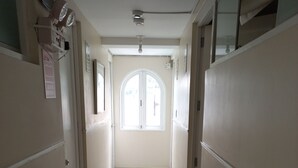 Um corredor com chão de azulejos, paredes brancas e uma grande janela em arco no final.