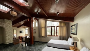 Quarto de hotel com duas camas, uma mesa de jantar, parede de pedra e grandes janelas com cortinas.