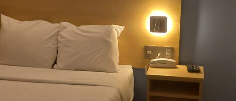 Quarto com cama, mesa de cabeceira com abajur e luminária na parede.