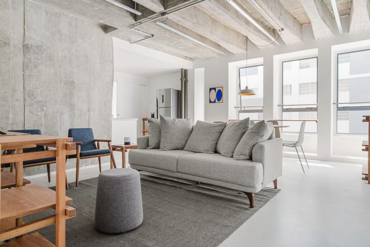 Uma sala de estar moderna com um sofá cinzento, cadeiras de madeira e um banquinho cinzento.