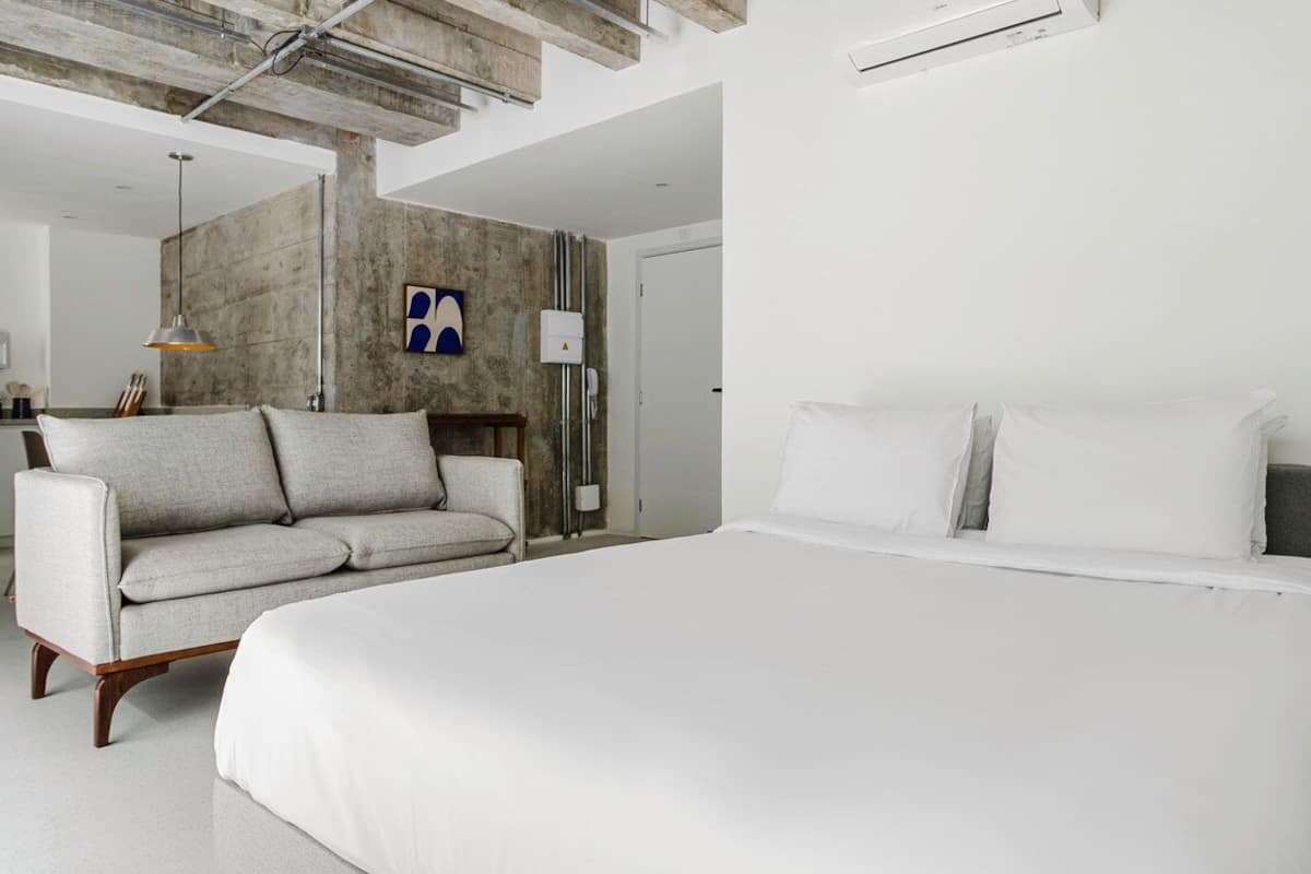 Quarto moderno com uma cama grande, um sofá e uma parede de destaque em concreto.