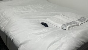 Cama bem arrumada com um controle remoto em cima, manta decorativa e três certificados emoldurados na parede.
