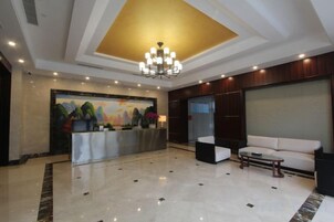 Um saguão de hotel com balcão de recepção, lustre, sofá e uma grande pintura na parede.