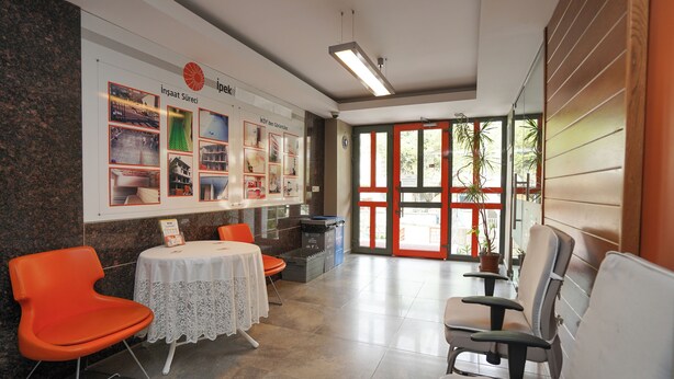 Uma área de recepção com balcão branco, cadeiras laranja e um painel de exposição com diversos cartazes informativos.