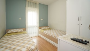 Quarto com duas camas, um guarda-roupa e um rack para TV com controles remotos.
