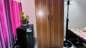 Quarto com guarda-roupa, cama, planta, lixeira e cabideiro.