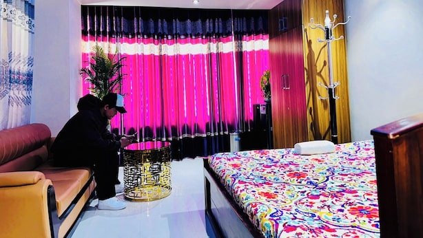 Quarto de hotel moderno com cama, sofá, abajur decorativo e cortinas.