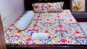 Uma cama com colcha florida, um travesseiro branco e outro a combinar em uma cabeceira de madeira.