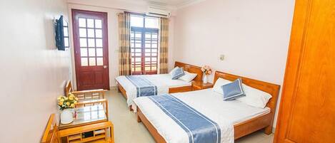 Quarto de hotel com duas camas, uma escrivaninha de madeira, uma cadeira e uma mesa pequena com um vaso de flores.