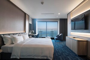 Quarto de hotel com uma cama grande, uma escrivaninha, uma cadeira, uma televisão e vista para a paisagem urbana.