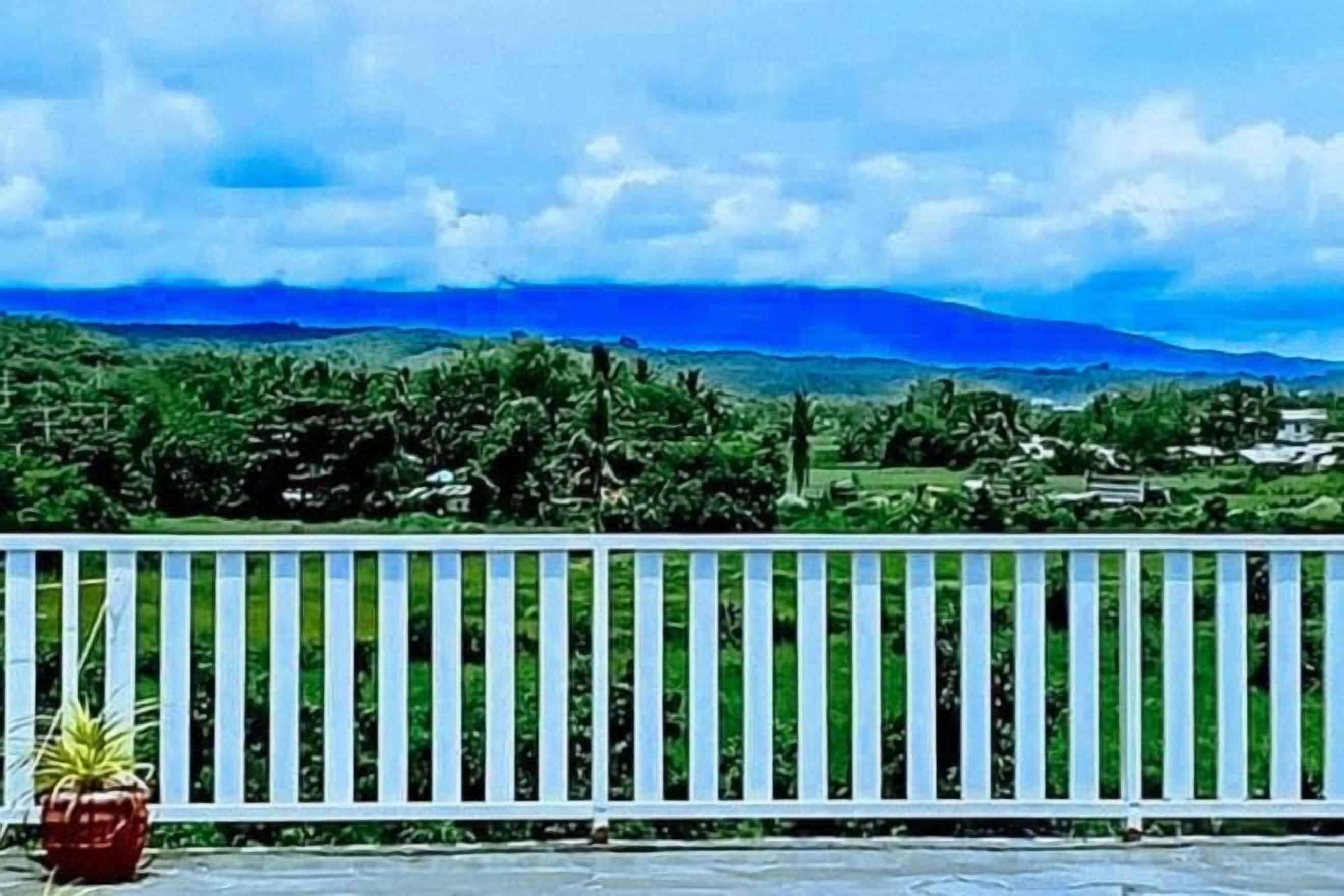 Varanda com guarda-corrimão branco, vista para paisagem verde com colinas e céu claro.