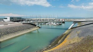 Marina com barcos atracados, um edifício moderno e um céu limpo.