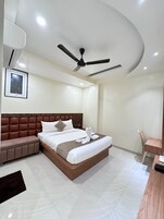 Quarto de hotel moderno com uma cama grande, um banco embutido, uma mesa de cabeceira de madeira e um ventilador de teto.