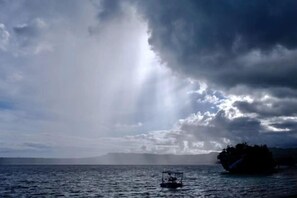 Um barco em águas calmas, com uma grande formação rochosa ao longe e céu nublado.
