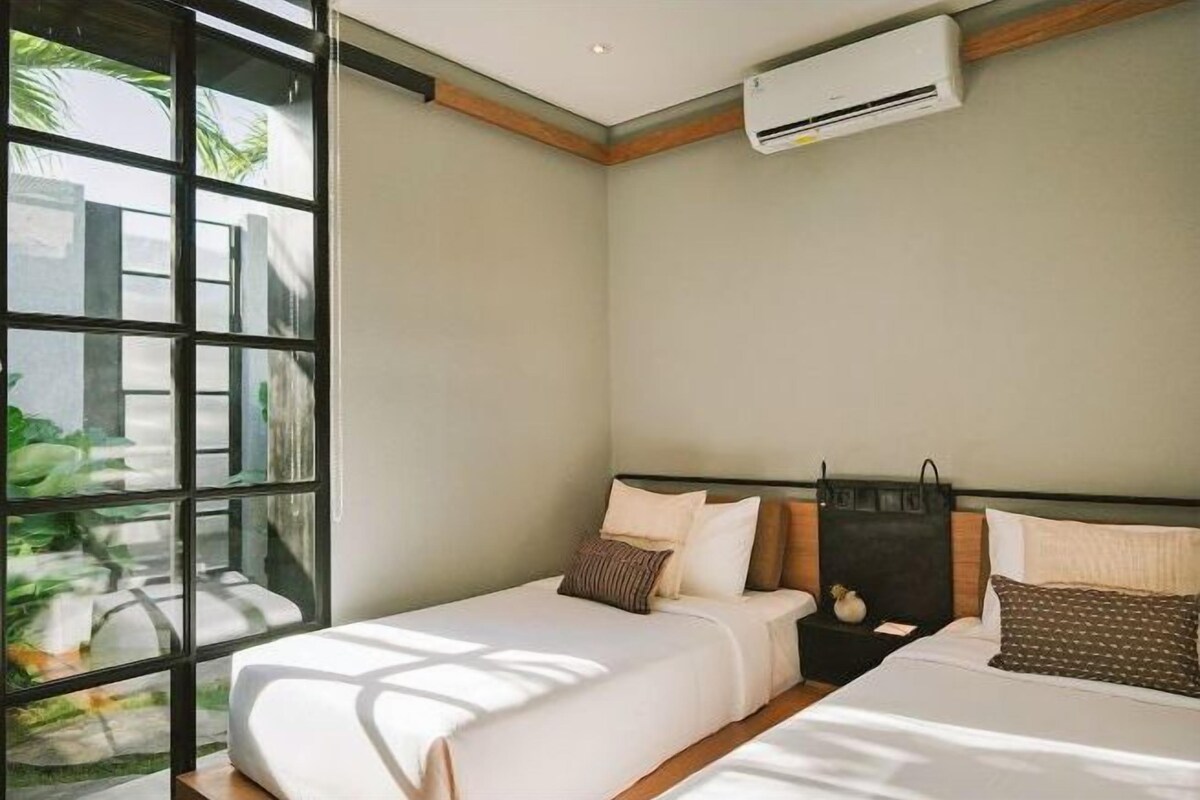 Quarto de hotel com duas camas, uma janela e um ar condicionado.