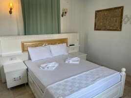 Quarto de hotel com uma cama branca, duas mesas de cabeceira, um criado-mudo, uma luminária na parede e um quadro emoldurado.