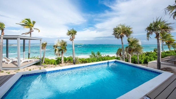 Piscina com vista para o oceano, rodeada por palmeiras e um gazebo.