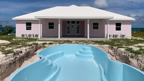 Uma casa rosa de dois andares com varanda frontal e piscina em primeiro plano.