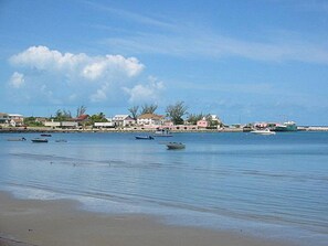 Uma vila costeira com uma praia de areia, águas calmas e vários barcos.