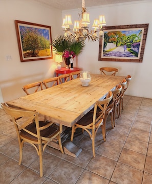 Uma sala de jantar com mesa de madeira, cadeiras, um candelabro e duas pinturas nas paredes.