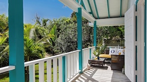 Um deck de madeira com guarda-corrimão branco, um banco e uma mesa com um vaso de planta.