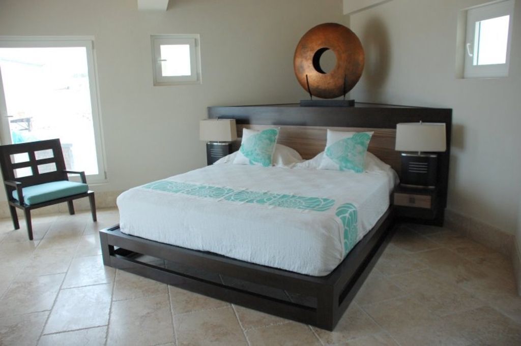 Quarto com uma cama, duas mesas de cabeceira, uma cadeira e um objeto decorativo grande na cabeceira.