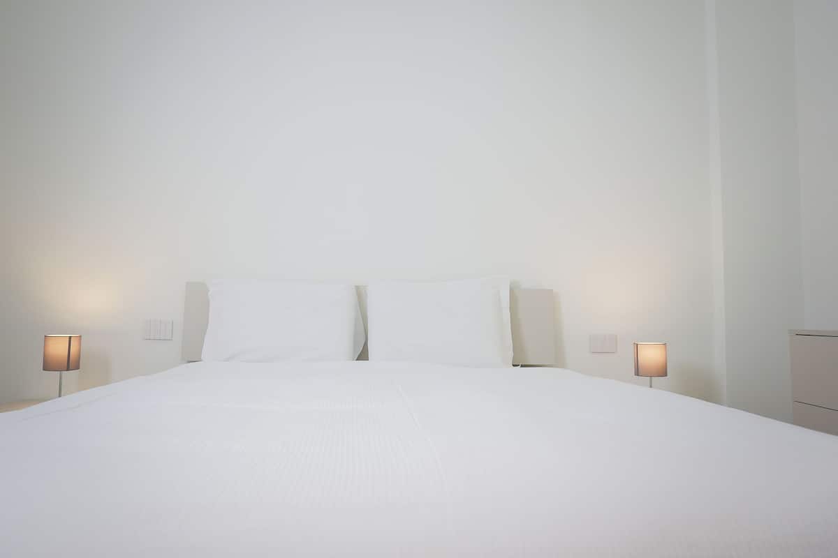 Quarto de hotel minimalista com uma cama grande, duas mesas de cabeceira e uma mesinha de apoio.