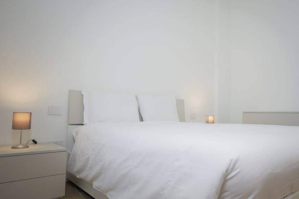 Quarto minimalista com uma cama de casal, duas mesas de cabeceira e duas luminárias fixadas na parede.